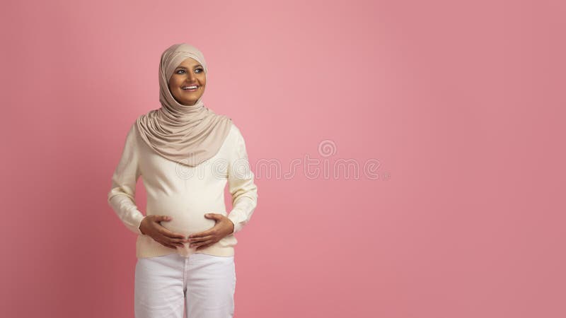 Smiling Pregnant Muslim Lady In Hijab Touching Belly And Looking Aside