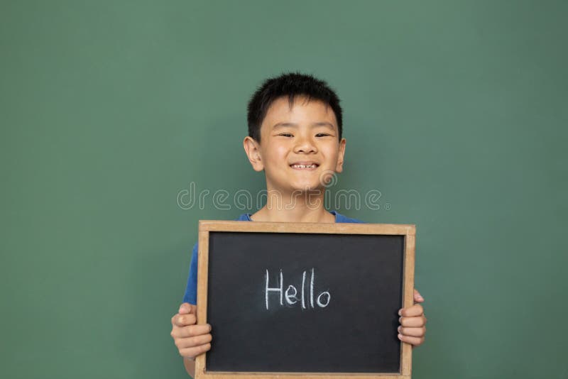 Smiling Schoolboy Standing and Holding a Hello Slate in a Classroom ...