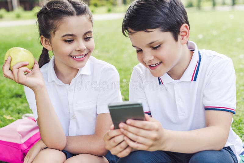 Smiling Schoolchildren Using Smartphone Together while Sitting Stock ...