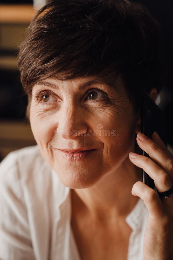 Smiling Mature Woman Talking On Cellphone While Sitting At Home Stock