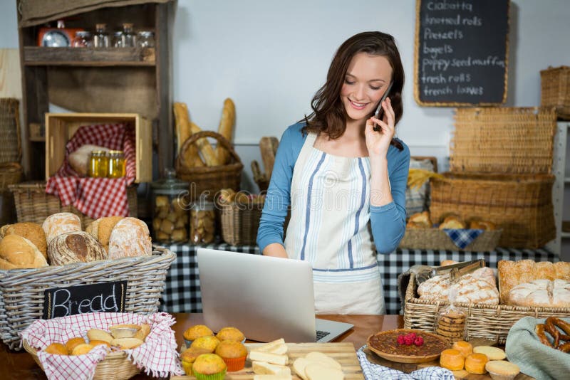 Smiling Staff Using Laptop while Talking on Mobile Phone at Bakery ...
