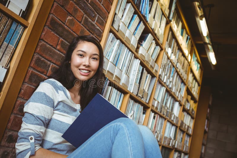 Smiling Student Sitting on the Floor Against Wall in Library Reading ...