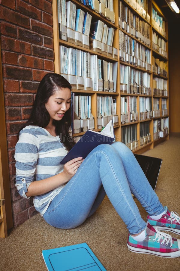 Smiling Student Sitting on the Floor Against Wall in Library Reading ...