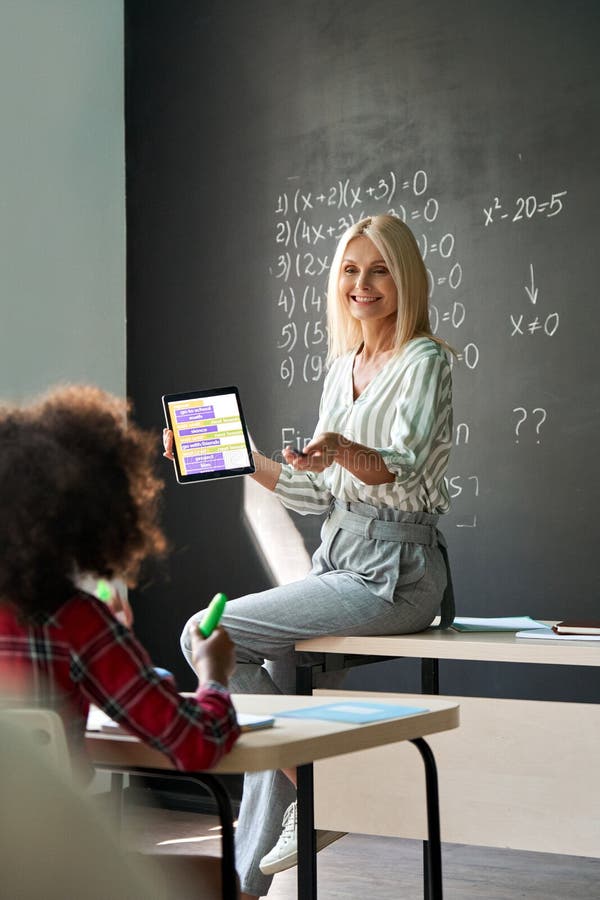 Smiling Teacher Having Maths Class Sitting on Desk Holding Tablet ...