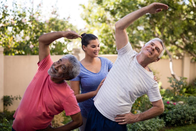 Smiling Trainer Guiding Senior Men during Exercise Stock Photo - Image ...