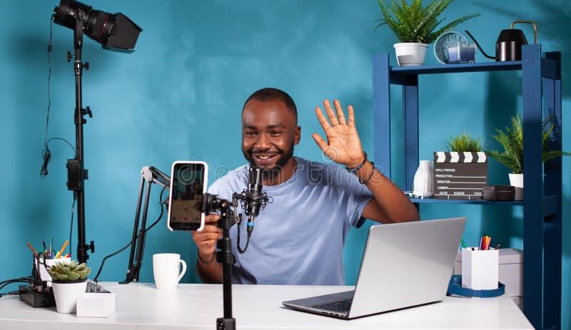 Smiling Vlogger Waving Hello in Front of Recording Smartphone Sitting ...