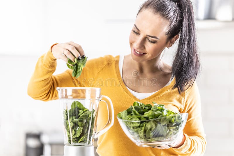 Smiling Woman Making Spinach Smoothie Putting Leaves In Blender Stock