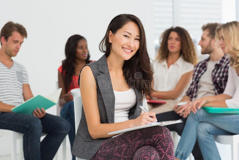 Smiling Woman Taking Notes while Colleagues are Talking Behind Her ...