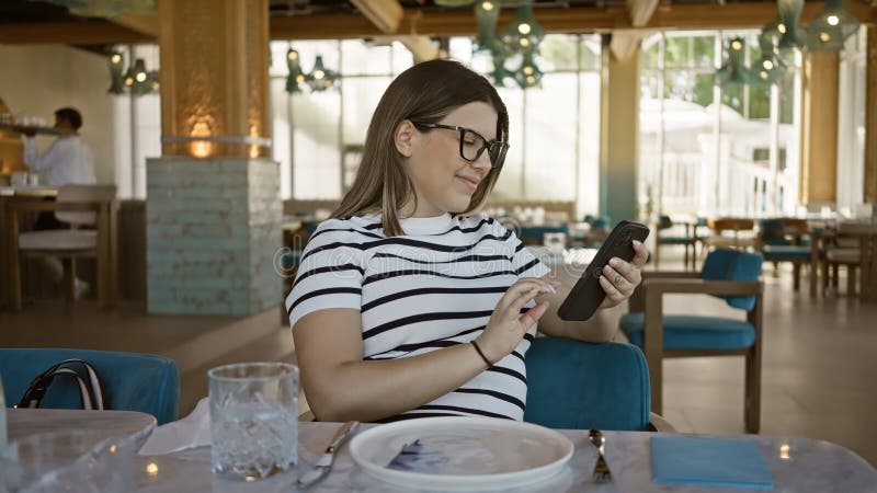 A Smiling Woman Uses a Smartphone while Sitting at a Table in a Modern ...
