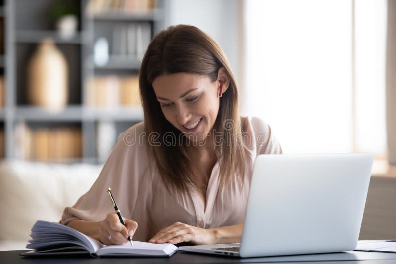 Smiling Woman Writing in Notebook, Using Laptop at Home Stock Image ...