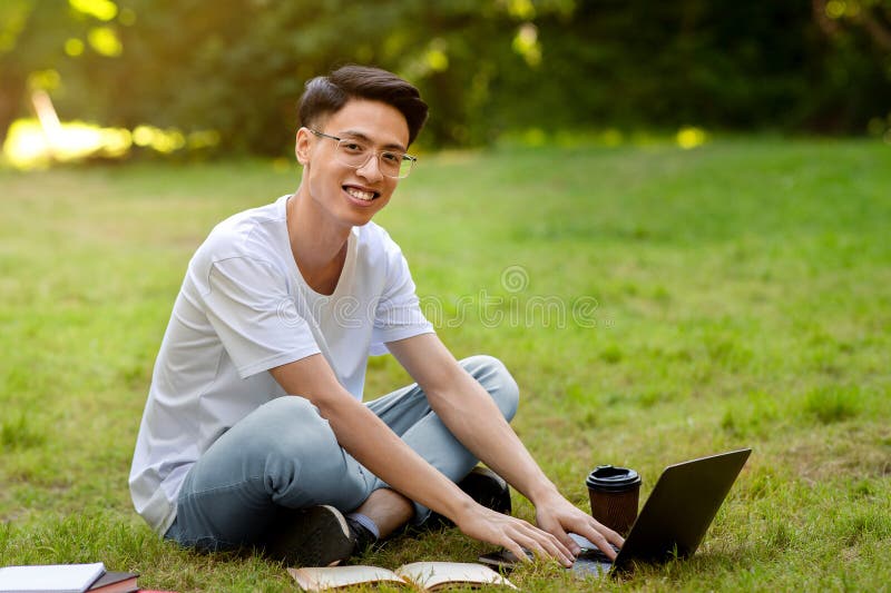 Smiling Young Asian Guy Sitting on Grass with Computer, Studying ...
