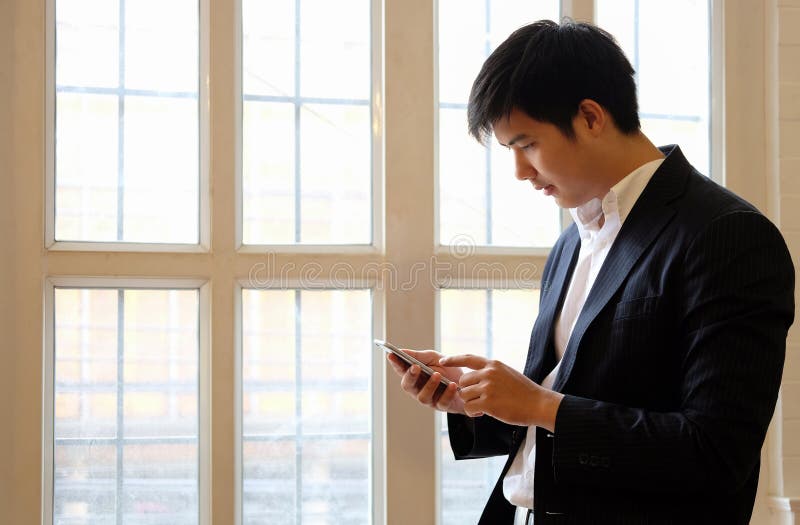Smiling Young Asian Man Using Smartphone while Standing Against Wall ...