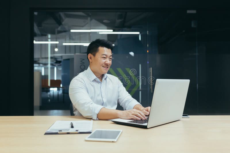 A Smiling Young Asian Man is Working in the Office on a Laptop. Sitting ...