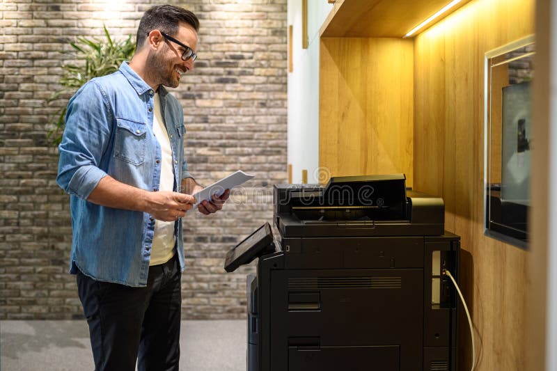 Smiling Young Businessman in Glasses Using Computer Printer for ...