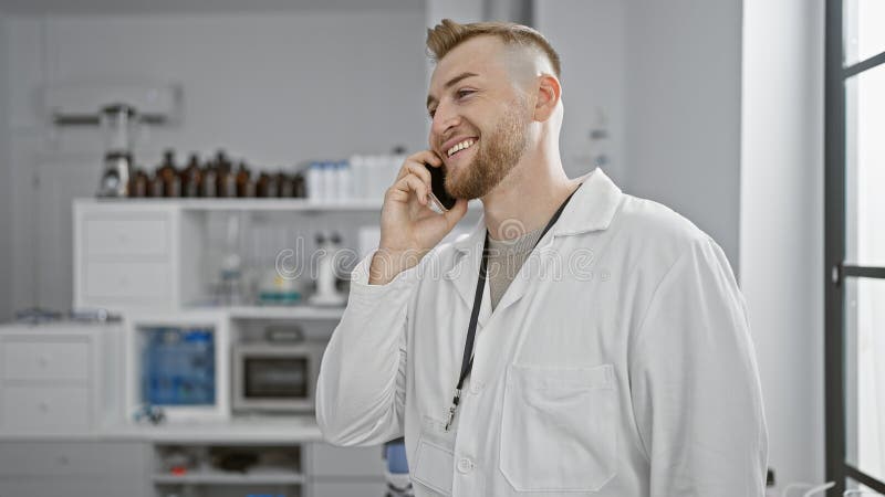 A Smiling Young Caucasian Man in a White Lab Coat Talking on a Phone in ...