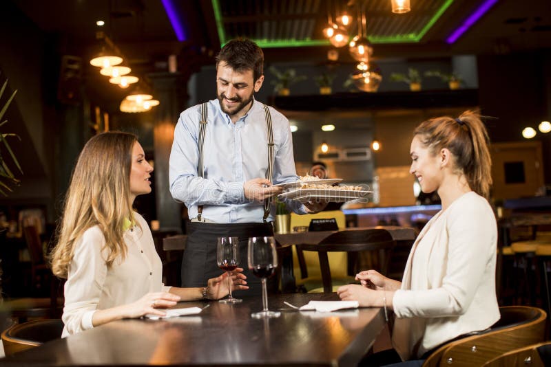 Smiling Young Female Friends at a Restaurant with Waiter Serving Dinner ...