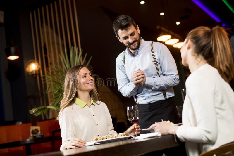 Smiling Young Female Friends at a Restaurant with Waiter Serving Dinner ...