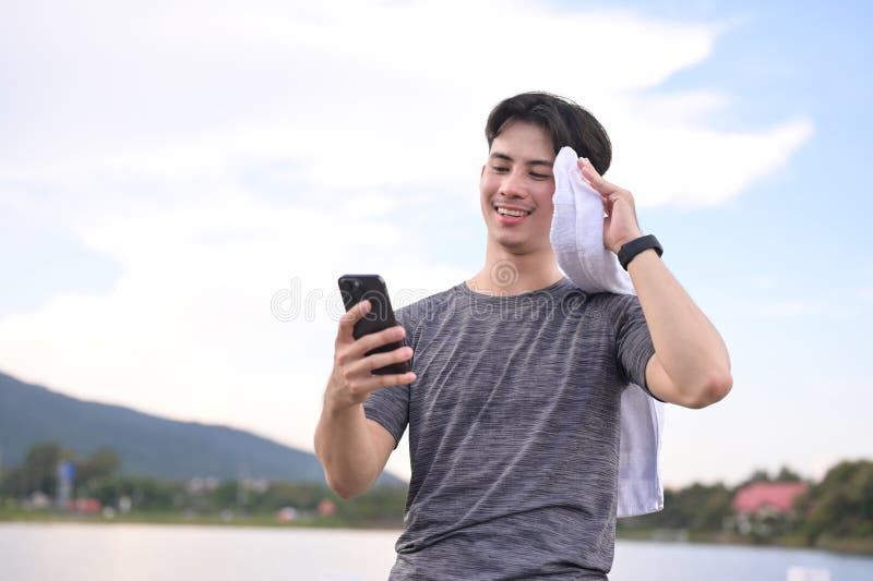 Smiling Young Male Runner Resting and Using Mobile Phone in the Park ...