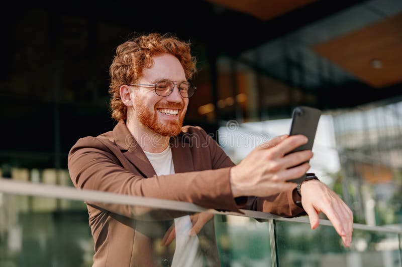 A Smiling Young Man is Happily Using His Smartphone Against the ...