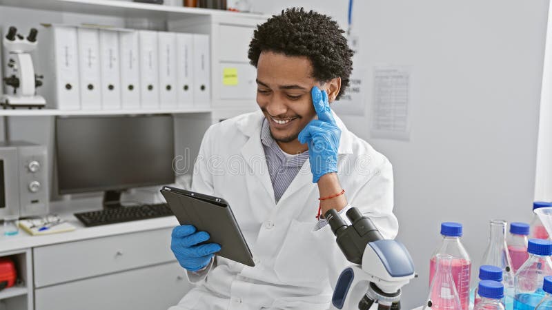 A Smiling Young Man in Lab Coat Using Tablet in Modern Laboratory ...