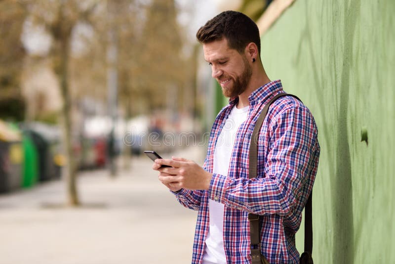 Smiling Young Man Looking His Smart Phone in Urban Background. L Stock ... Smiling Young Man Looking His Smart Phone in Urban Background. L Stock ...