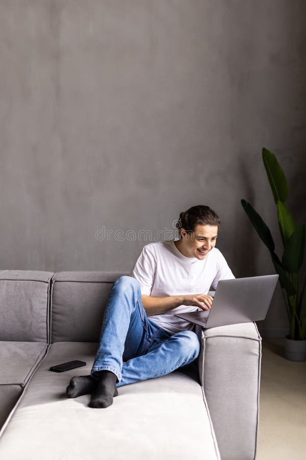 Smiling Young Man Sitting on a Couch at Home, Using Laptop Stock Photo ...