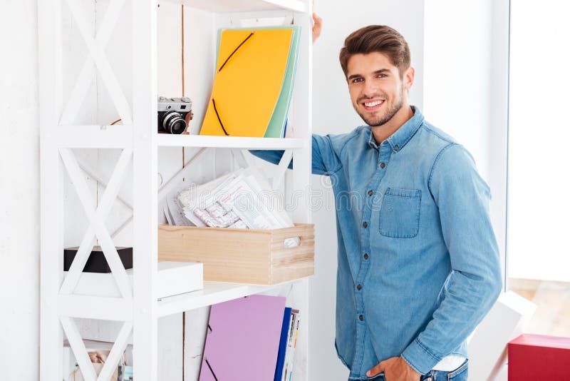 Smiling Young Man Standing at Shelf with Folders and Documents Stock ...