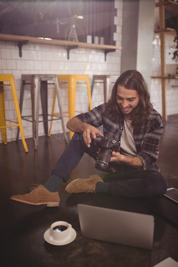 Smiling Young Man Using DSLR Camera while Sitting with Laptop on Floor ...