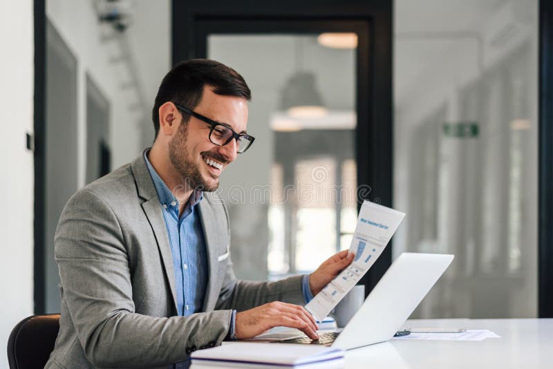 Smiling Young Professional Working on Laptop while Reading Documents at ...