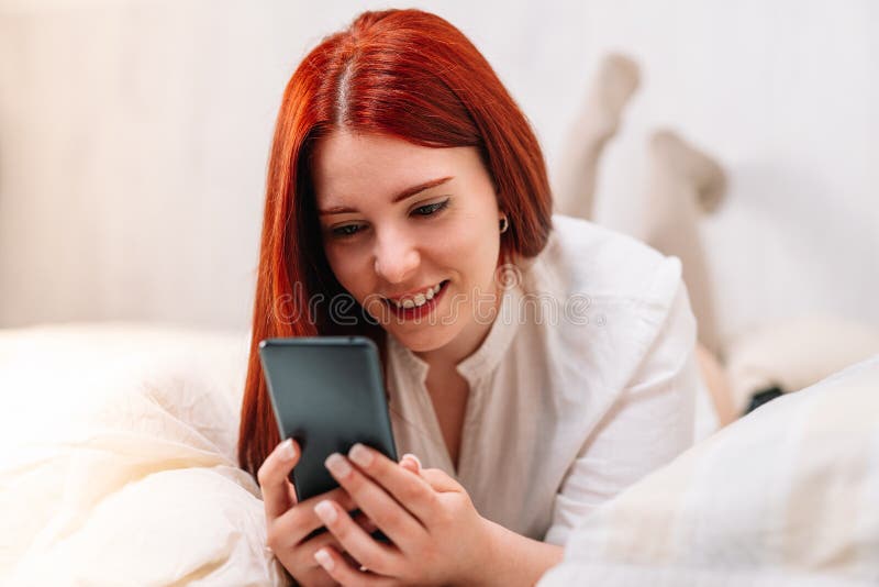 Smiling Young Woman Chatting On Her Cell Phone Lying On Her Bedroom