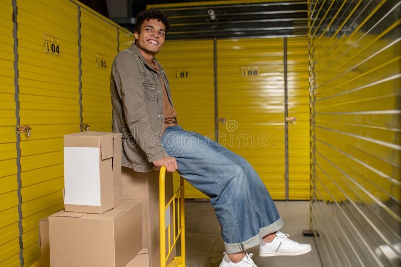 Smiling Young Warehouse Worker Sitting on the Box and Resting Stock ...