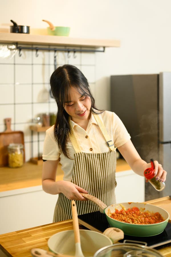 Smiling Young Woman Adding Spices into a Simmering Pan of Tomato Based ...