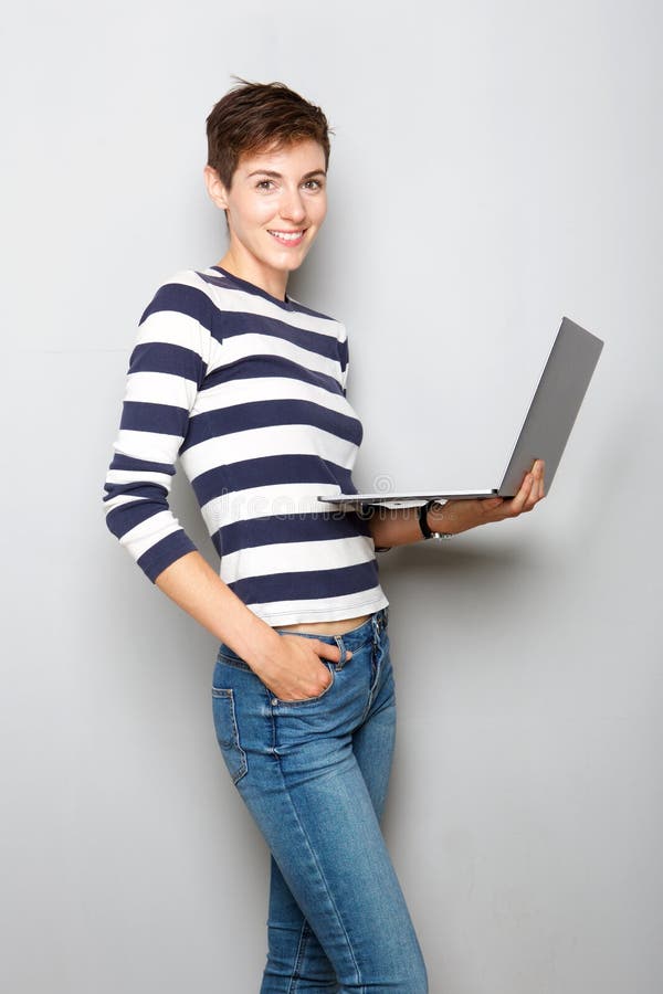 Smiling Young Woman Holding Laptop Computer Against Gray Background ... Smiling Young Woman Holding Laptop Computer Against Gray Background ...