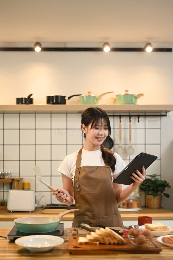 Smiling Young Woman Standing in a Kitchen, Following a Recipe or ...