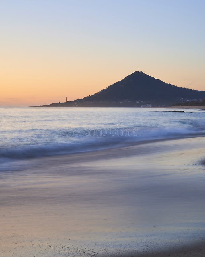 Smooth Waves Over a Sandy Beach at Sunset with Mountain in Background ...