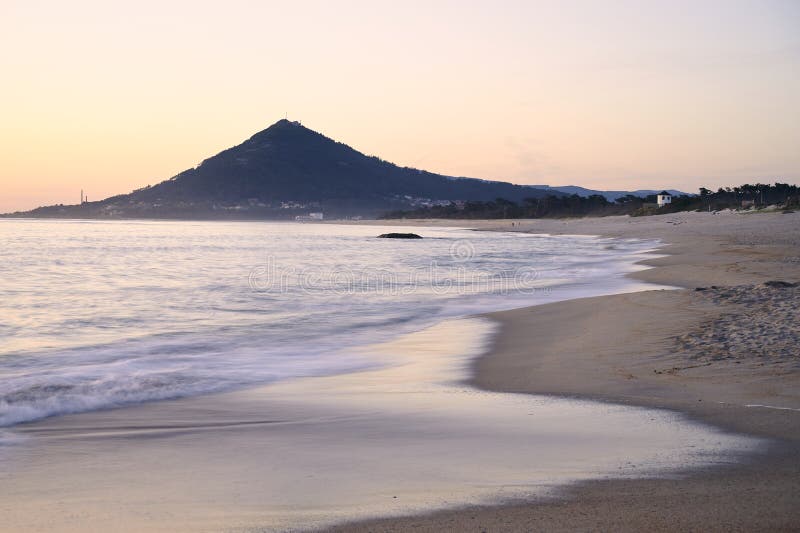 Smooth Waves Over a Sandy Beach at Sunset with Mountain in Background ...