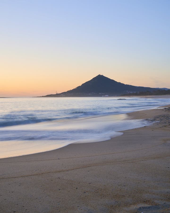 Smooth Waves Over a Sandy Beach at Sunset with Mountain in Background ...