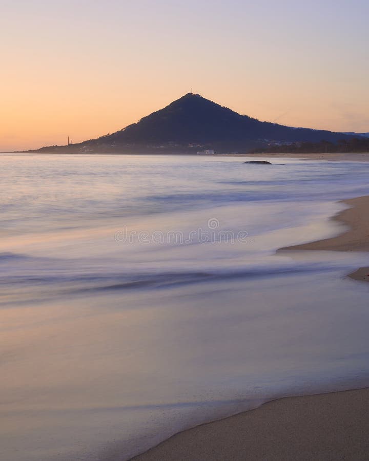 Smooth Waves Over a Sandy Beach at Sunset with Mountain in Background ...