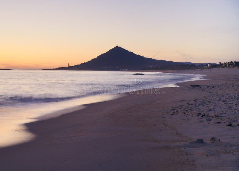 Smooth Waves Over a Sandy Beach at Sunset with Mountain in Background ...