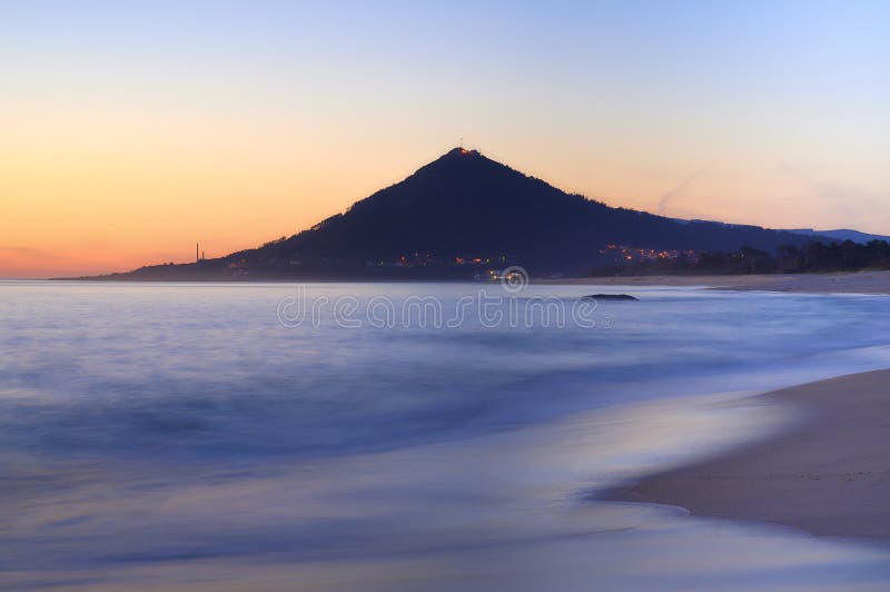 Smooth Waves Over a Sandy Beach at Sunset with Mountain in Background ...