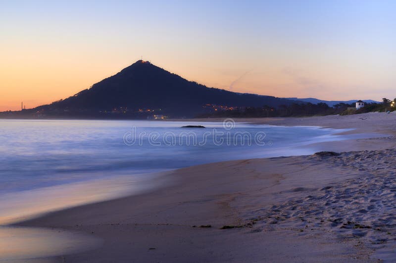 Smooth Waves Over a Sandy Beach at Sunset with Mountain in Background ...