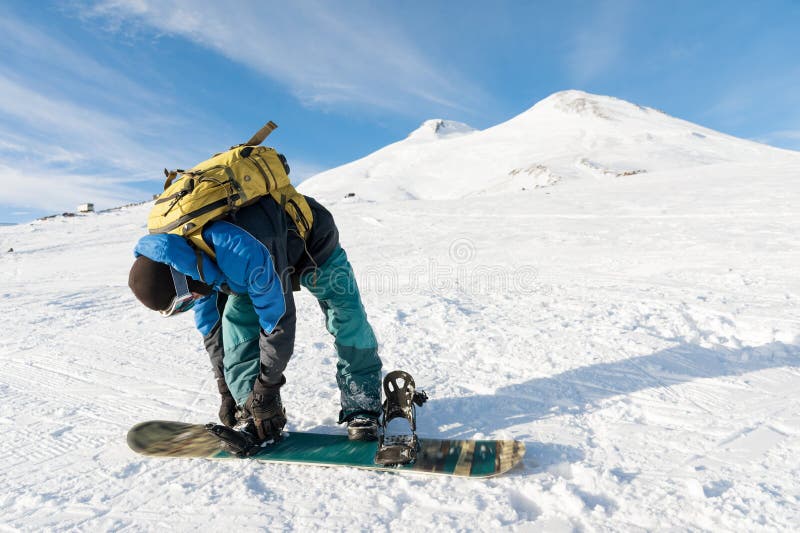 A Snowboarder with a Backpack on His Back Fastens Snowboard Bindings ...