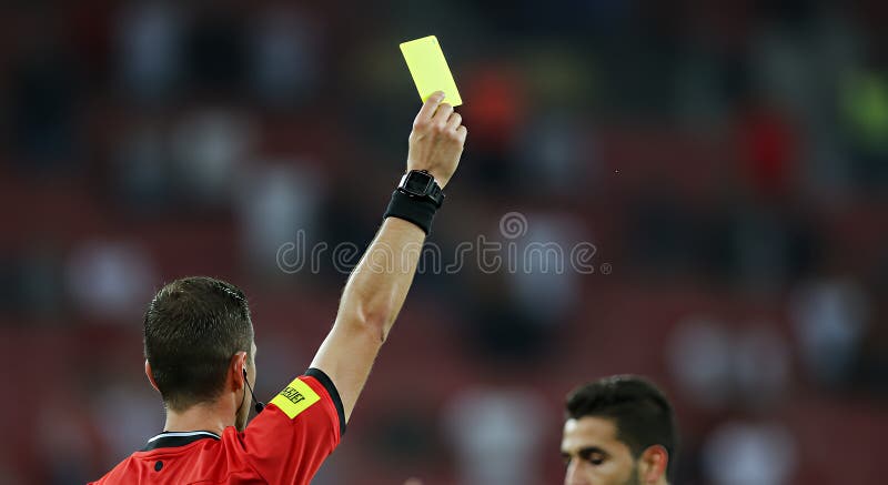 A Soccer Referee Holds Up a Bright Yellow Card in a Stadium Setting ...
