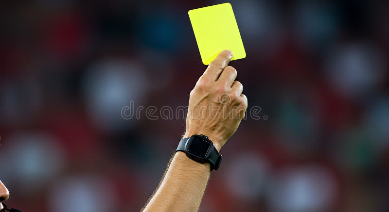 A Soccer Referee Holds Up a Bright Yellow Card in a Stadium Setting ...