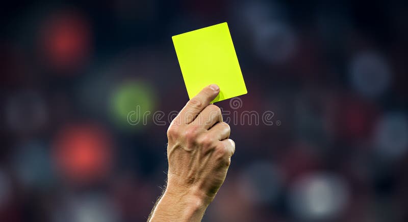 A Soccer Referee Holds Up a Bright Yellow Card in a Stadium Setting ...