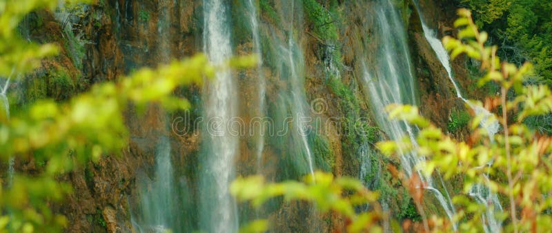 Soft Waterfalls Flow Down a Rocky Cliff Surrounded by Green Leaves in ...