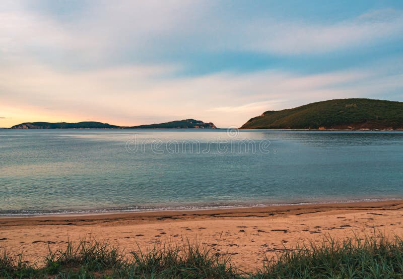Soft Waves Wash Over a Sandy Beach As the Sun Sets Behind Rolling Green ...