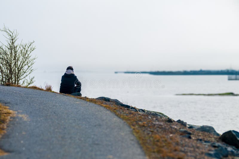 Solitary Figure Sitting by the Waterfront on a Cloudy Day.. Stock Photo ...