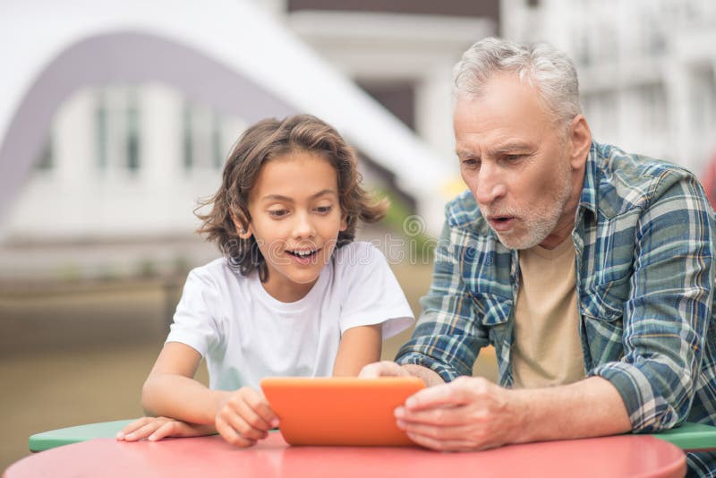Son and Dad Watching Something on a Tablet and Looking Involved Stock ...