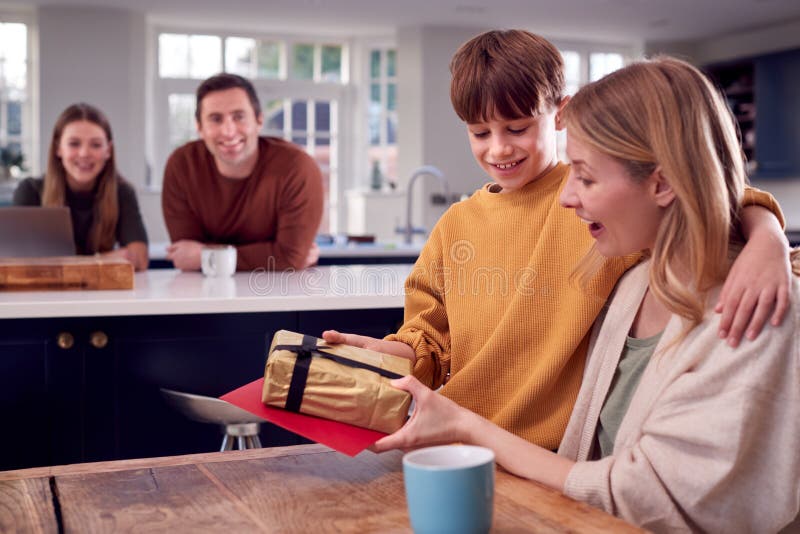 Son Giving Mother Gift As she Sits at Kitchen Table at Home Stock Image ...